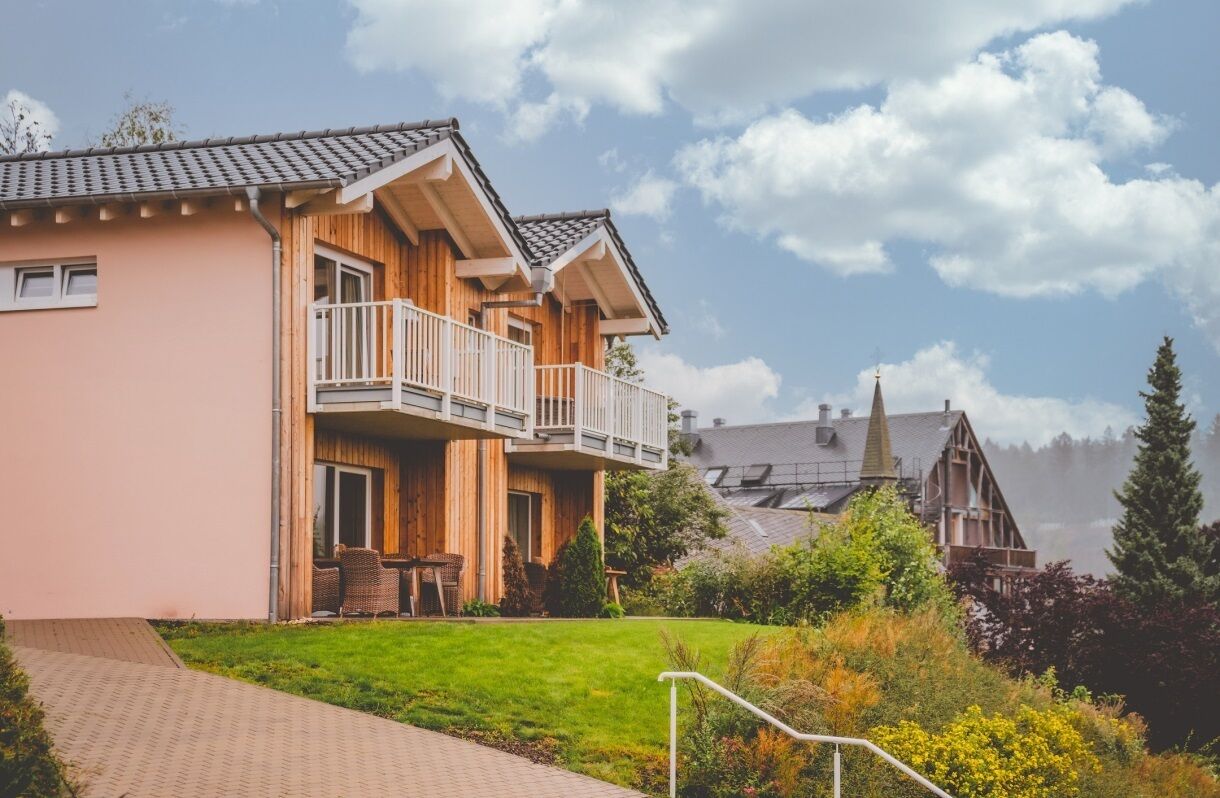 Uma casa de madeira de dois andares com varanda, entrada pavimentada e gramado.