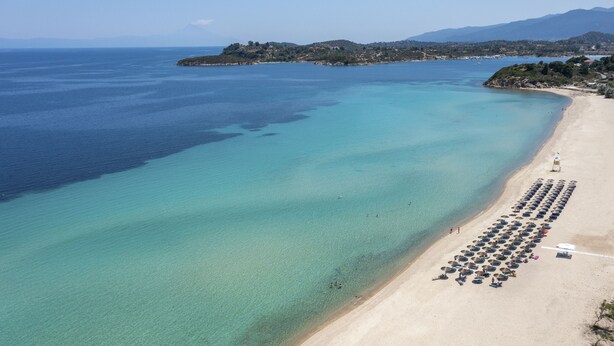 Vista aérea de uma praia com águas turquesa cristalinas, areal arenoso e uma fileira de guarda-sóis.