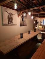 Um interior rústico com vigas de madeira, uma longa mesa de madeira e dois retratos emoldurados de animais.