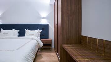 Quarto de hotel moderno com uma cama grande, uma mesinha de cabeceira de madeira e um banco embutido.