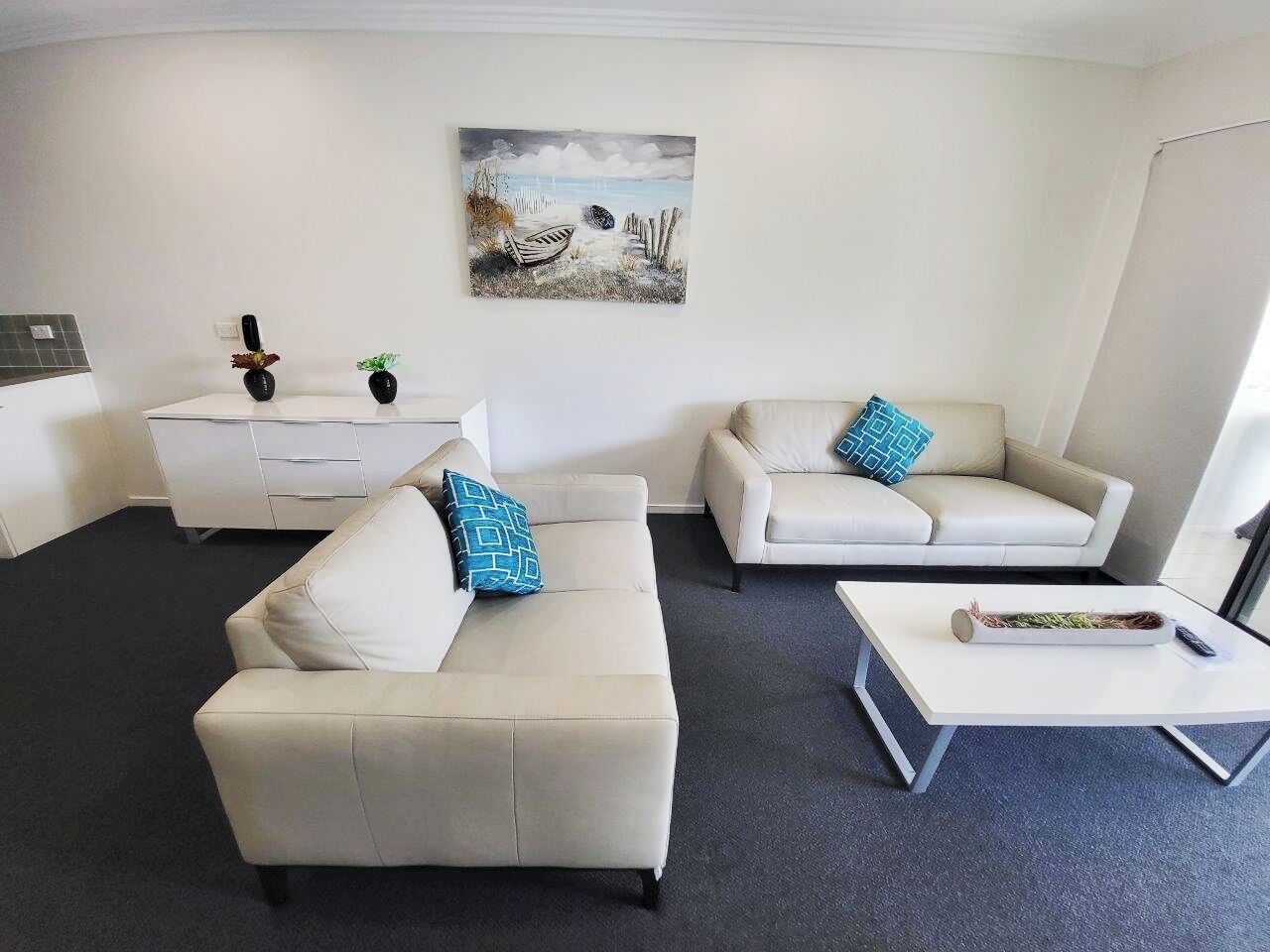 Uma sala de estar moderna com dois sofás brancos, uma mesa de centro e um quadro na parede.