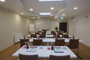Uma sala de conferências com mesas brancas, cadeiras marrons e um quadro branco.