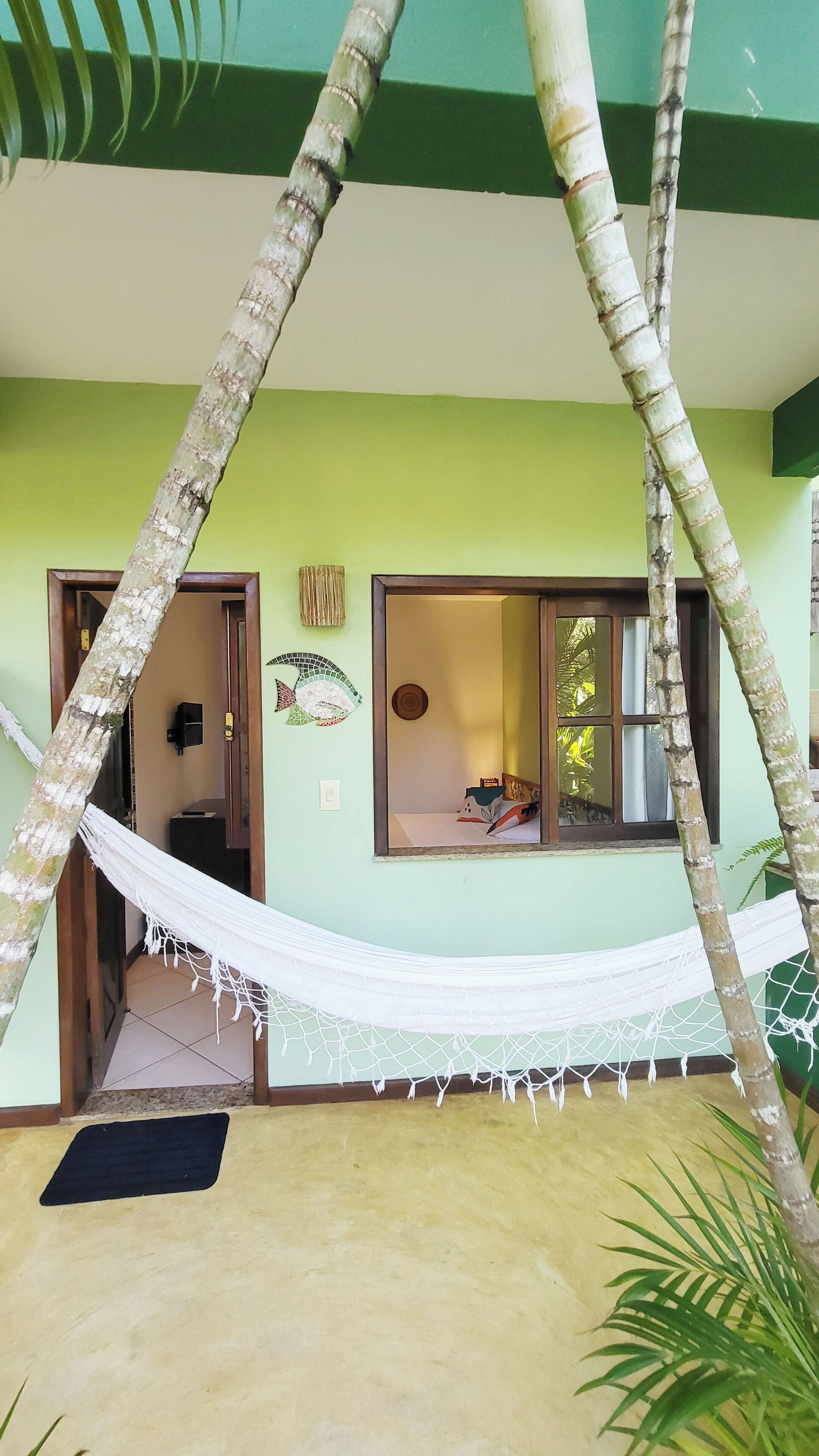 Quarto com rede, cama, janela com vista e porta para outro cômodo.