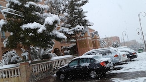 Rua urbana coberta de neve, com carros estacionados e árvores nevadas.
