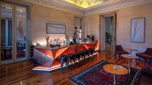 Uma área de bar com design moderno, incluindo um balcão e banquetas, num espaço com piso de madeira e teto decorativo.