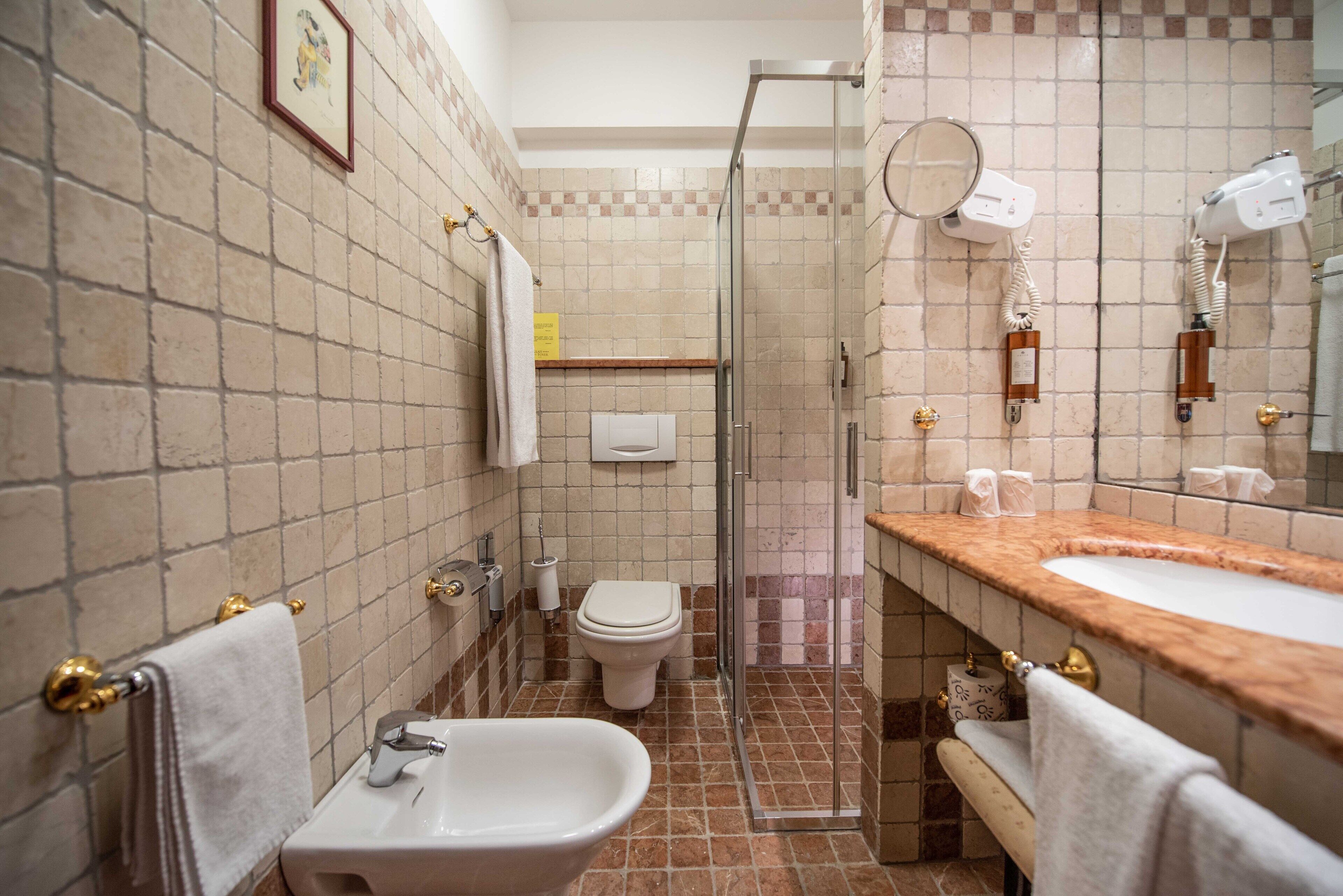Casa de banho com lavatório, bidé, sanita e cabine de duche com parede de vidro.