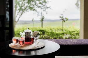 Uma mesa com bule, xícaras e um vaso de flores, com vista para o verde através de uma janela.