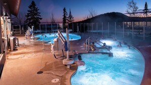 Uma área de piscina aquecida ao ar livre, com vários ofurôs e céu claro ao entardecer.