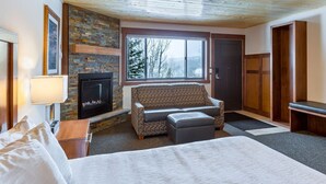 Quarto aconchegante com lareira, sofá, cama e uma grande janela com vista para árvores.