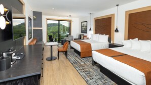 Quarto de hotel moderno com duas camas, uma escrivaninha e uma janela grande com vista para as montanhas.