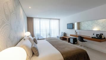 Quarto de hotel moderno com uma cama grande, uma escrivaninha, uma cadeira, uma televisão e um abajur.