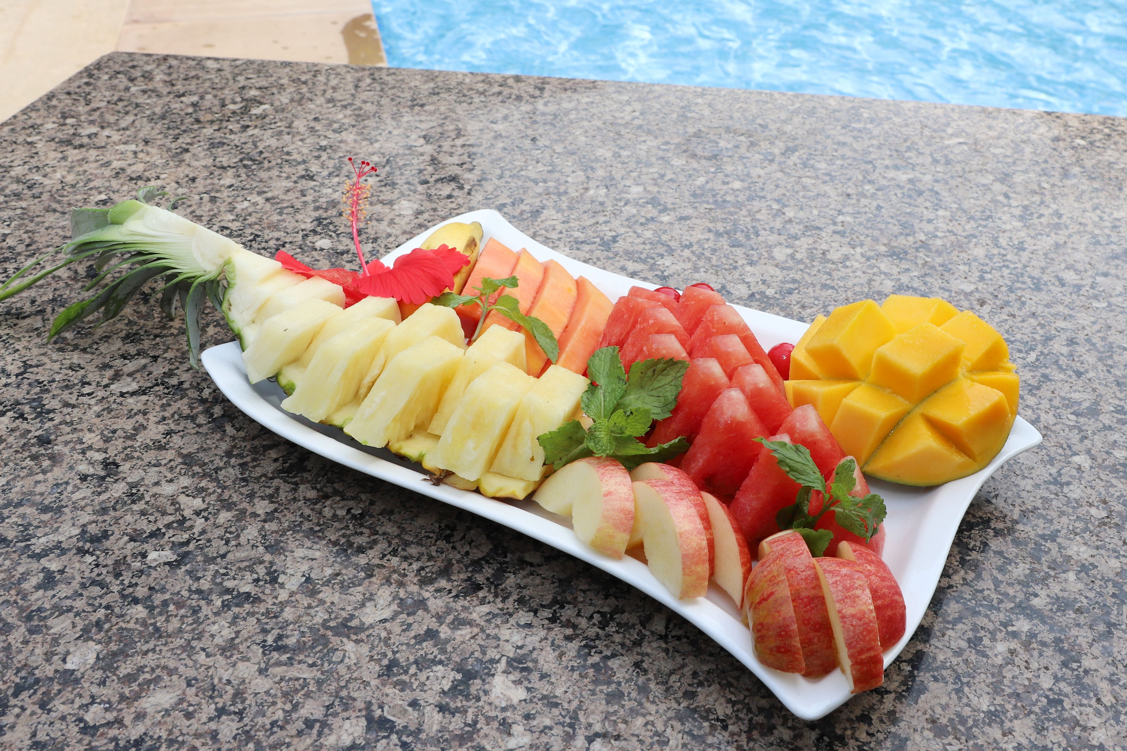 Uma tábua de frutas sobre uma mesa de granito perto de uma piscina.