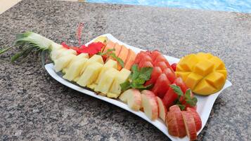 Uma tábua de frutas sobre uma mesa de granito perto de uma piscina.