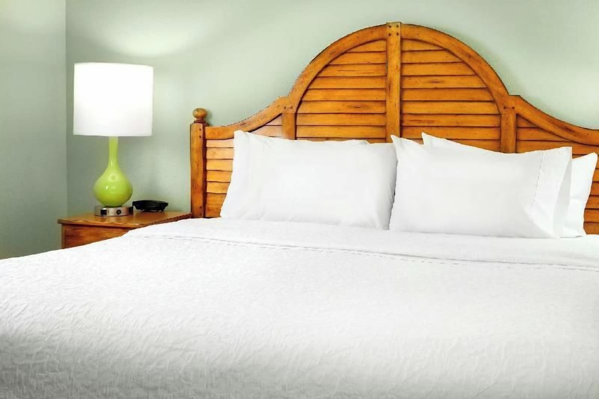 Uma cama com cabeceira de madeira, luminária verde e travesseiro branco.