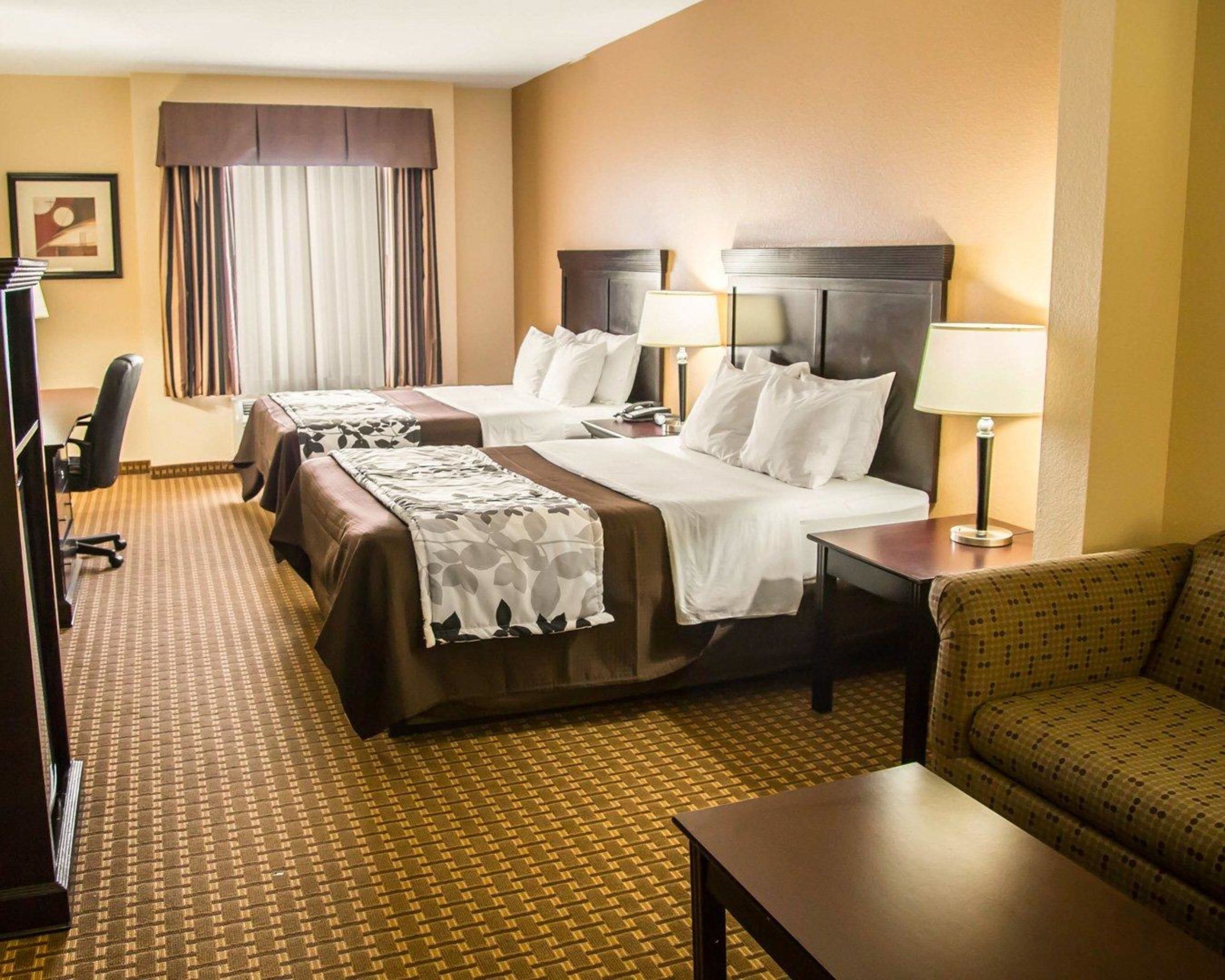 Quarto de hotel com duas camas, uma escrivaninha, uma cadeira e um sofá.