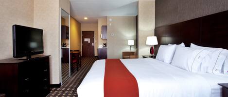 Quarto de hotel com uma cama grande, televisão em uma cômoda, escrivaninha com abajur e vista para o corredor.