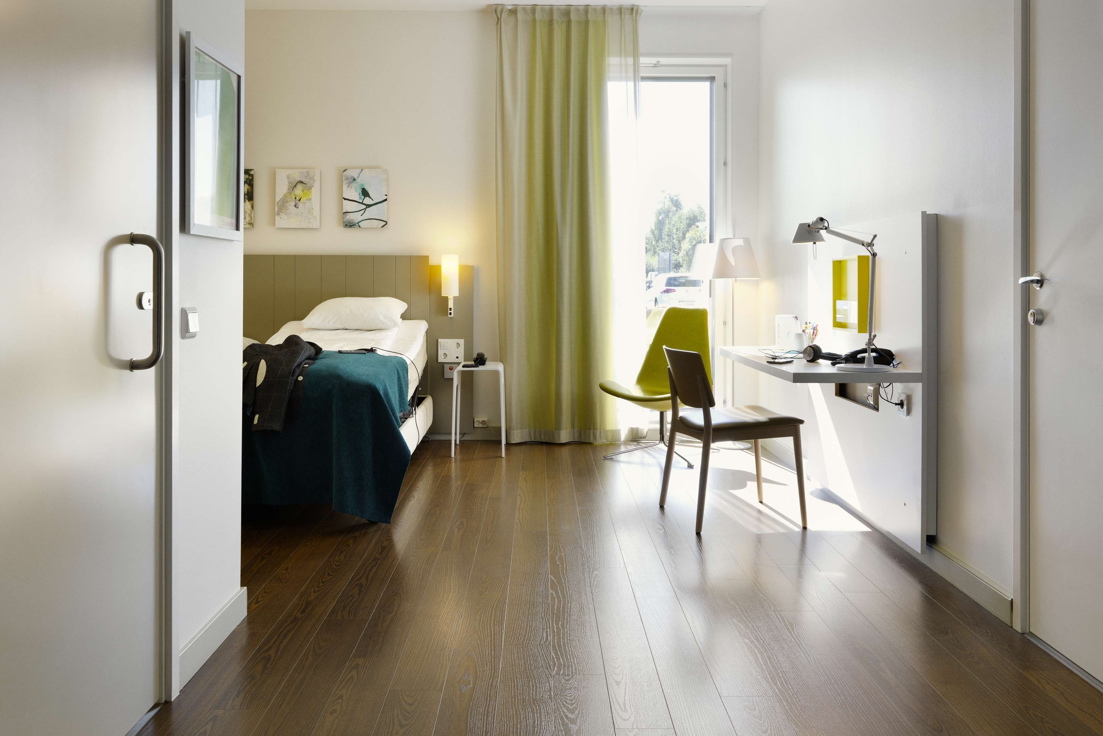 Quarto de hotel com cama, escrivaninha, cadeira e vista para o exterior.