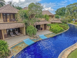 Um resort com piscina, construções com telhados de palha e vegetação exuberante.