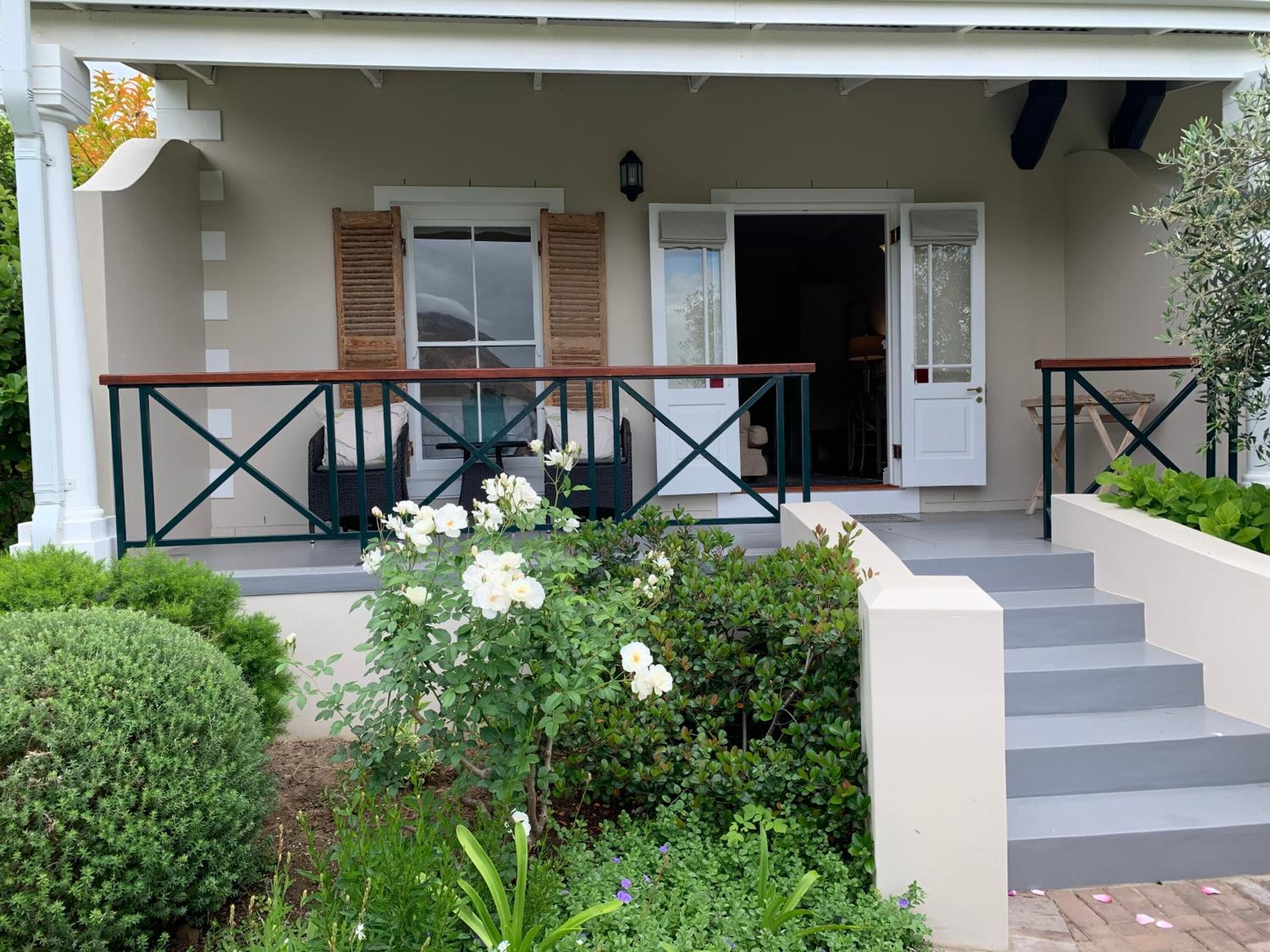 Uma área externa coberta com uma escadaria que leva a uma porta, cercada por vegetação e um pequeno jardim.