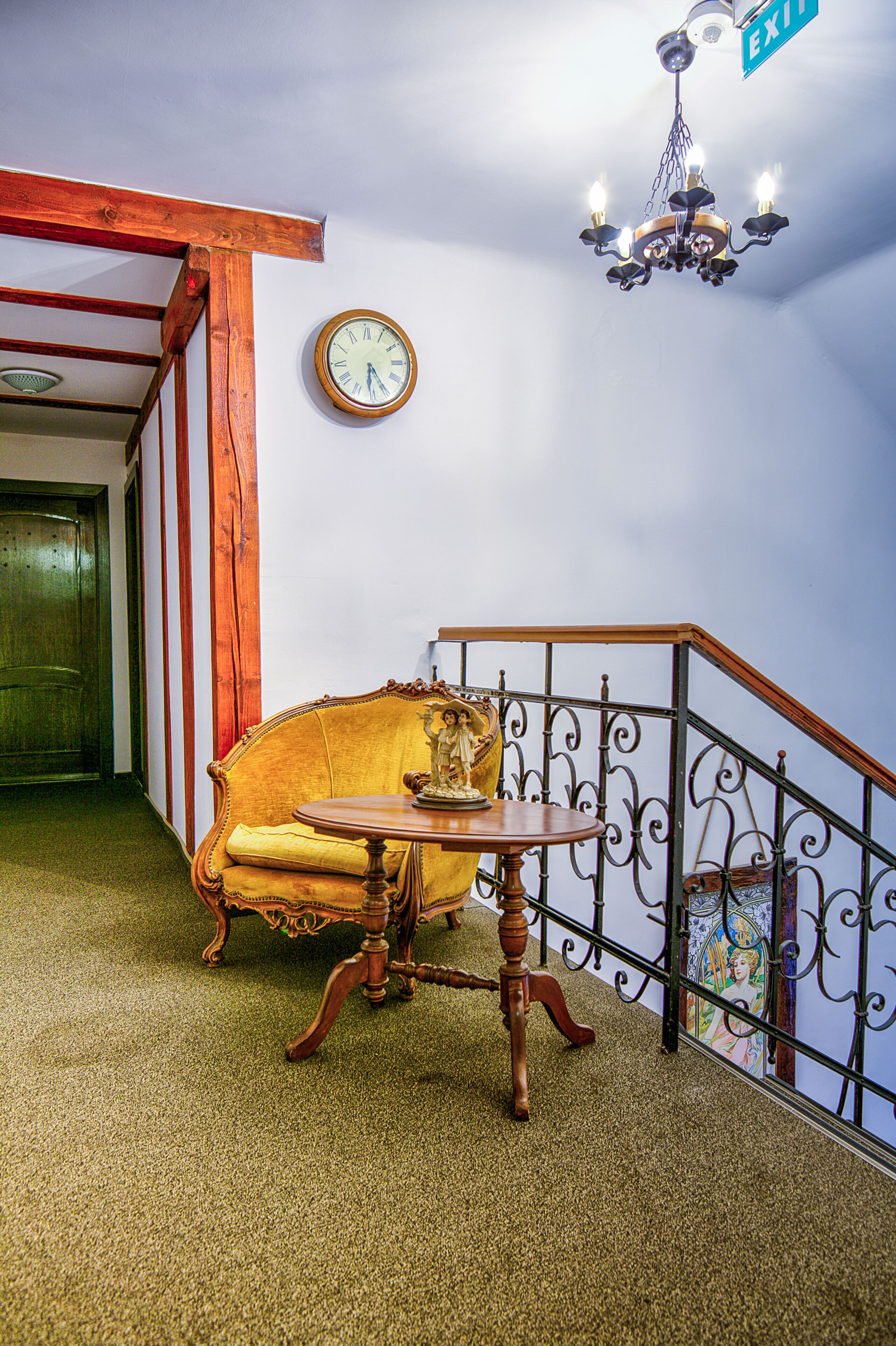 Quarto com cadeira de madeira, uma pequena mesa, relógio de parede e um candelabro.