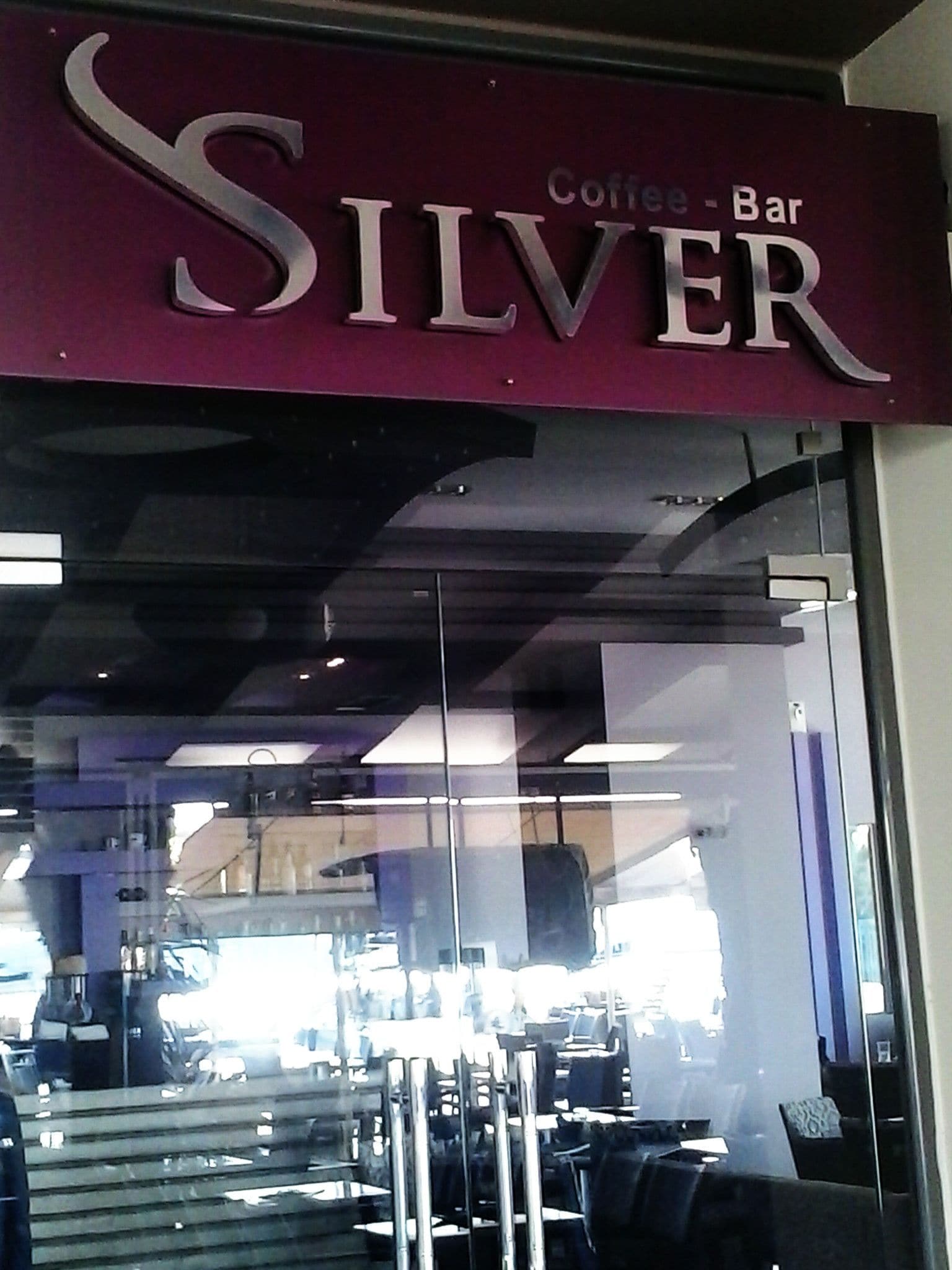 Um café chamado 'SILVER', com entrada de vidro e área de estar visível no interior.