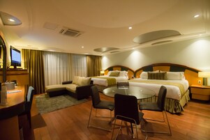 Quarto de hotel com uma cama grande, duas camas menores, uma mesa de jantar de vidro e um sofá.