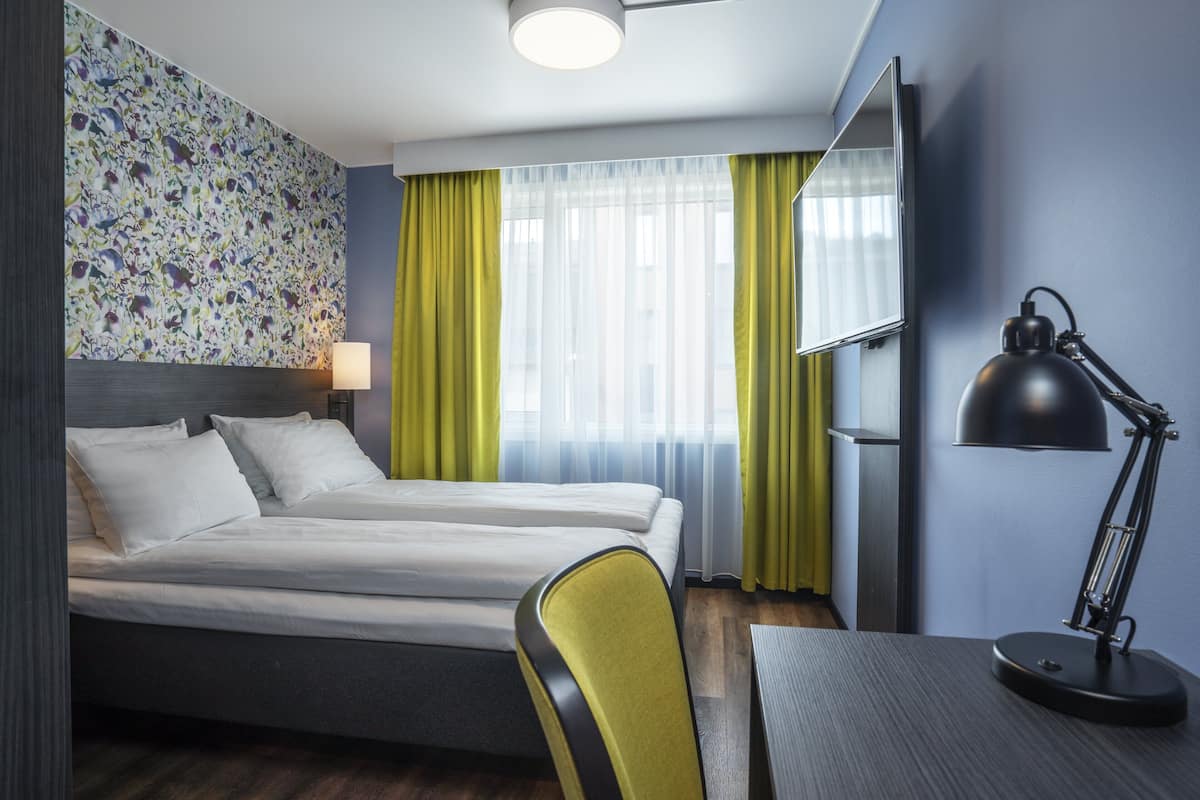 Quarto de hotel com cama, escrivaninha com luminária e cadeira.