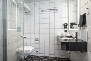 Uma casa de banho moderna com cabine de duche em vidro, sanita branca, lavatório preto com espelho e porta-toalhas.