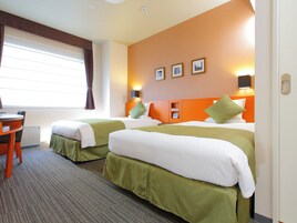 Quarto de hotel com duas camas, uma escrivaninha e janela com cortinas.
