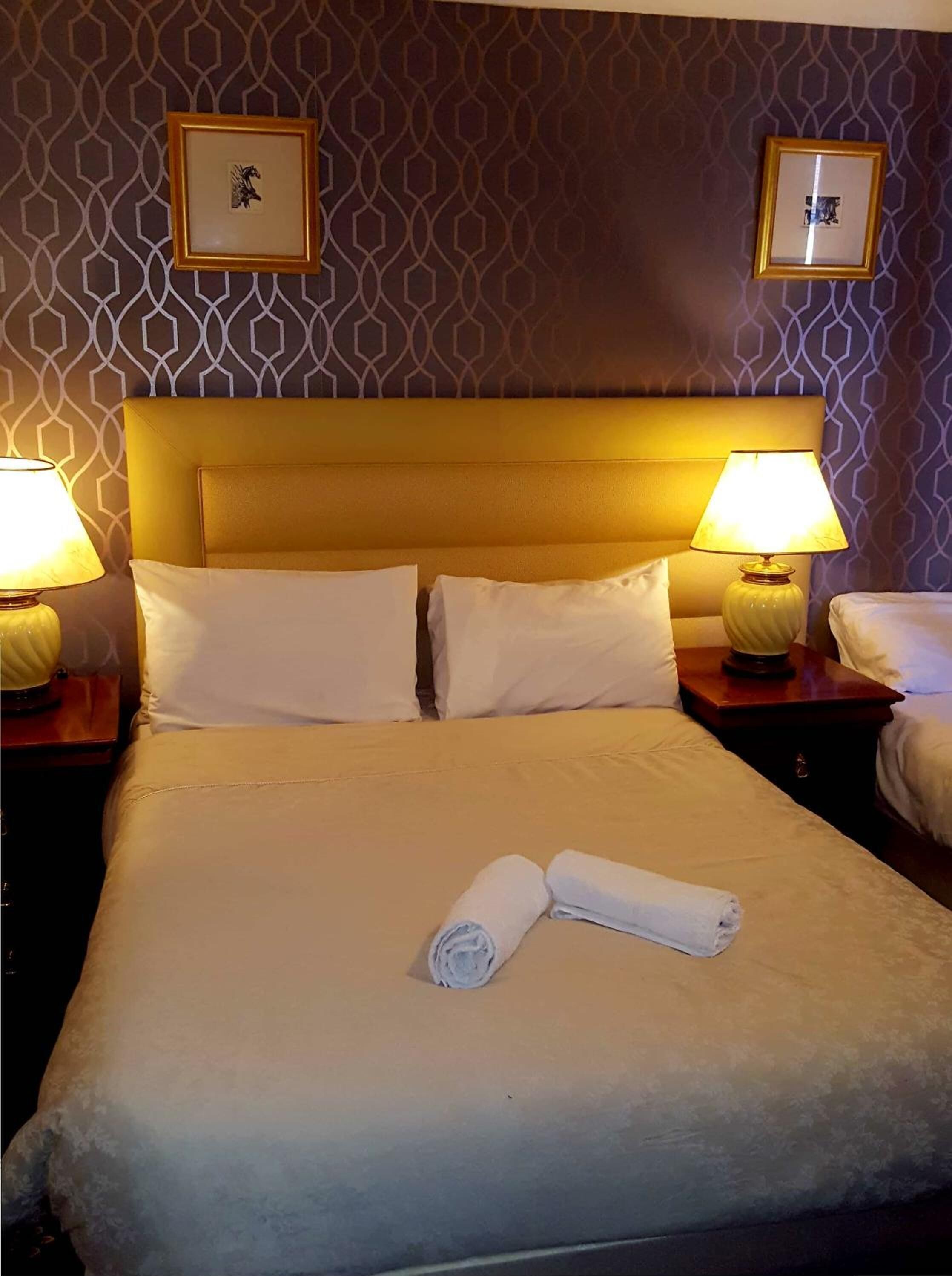 Quarto de hotel com uma cama grande, duas luminárias de cabeceira e duas fotos emolduradas na parede.