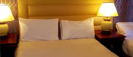 Quarto de hotel com uma cama grande, duas luminárias de cabeceira e duas fotos emolduradas na parede.