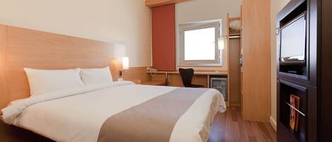 Quarto de hotel com uma cama grande, uma escrivaninha, uma cadeira, um guarda-roupa e uma televisão.
