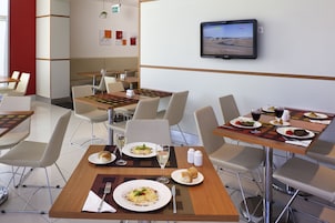 Uma sala de jantar moderna com várias mesas, cadeiras e uma televisão de tela plana na parede.