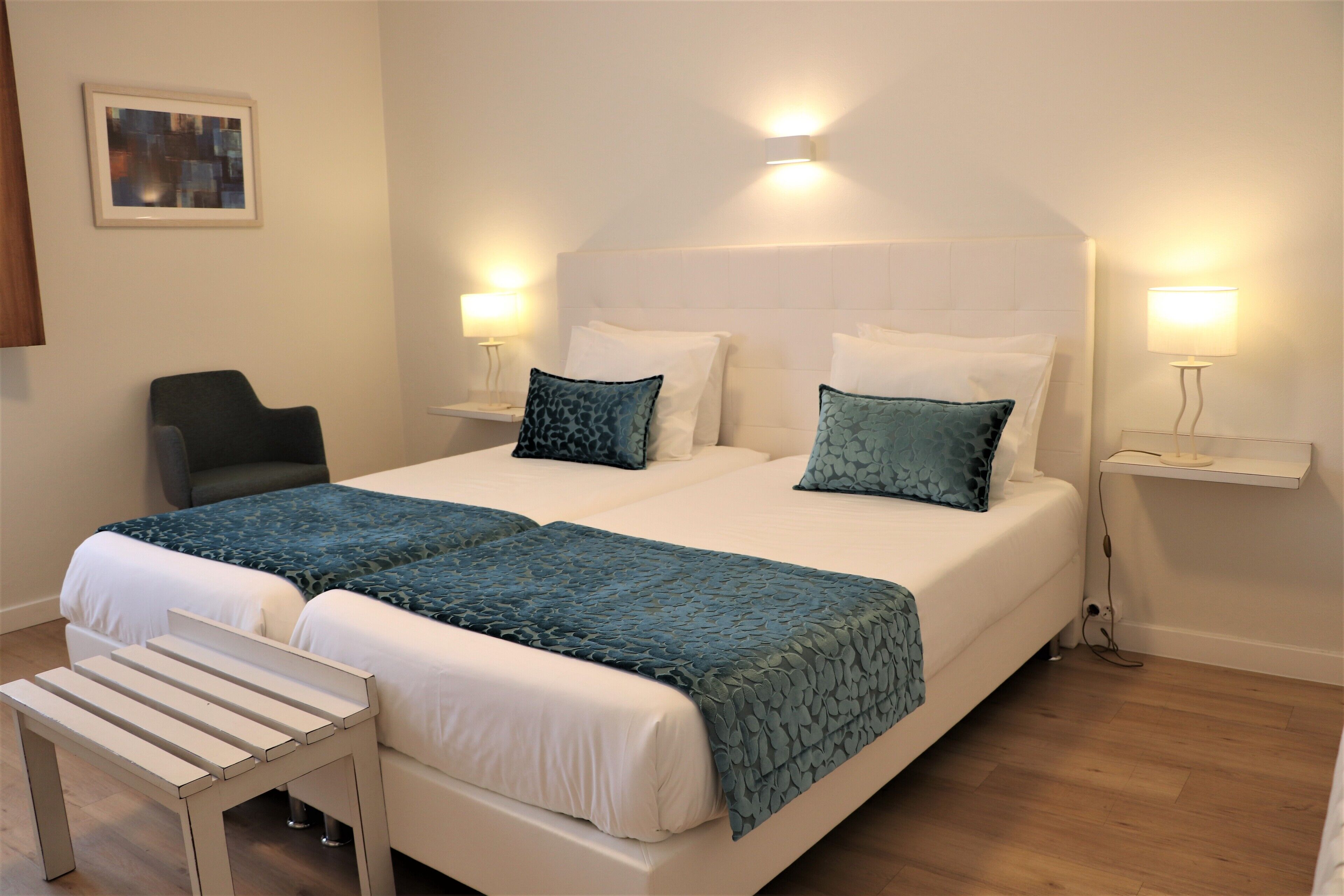 Cama de casal com duas almofadas, mesa de cabeceira, uma cadeira e abajur.