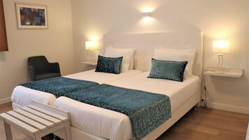 Cama de casal com duas almofadas, mesa de cabeceira, uma cadeira e abajur.