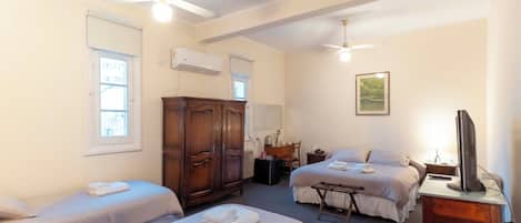 Quarto de hotel com duas camas, um guarda-roupa de madeira, uma escrivaninha com computador e ventoinhas de teto.