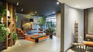 Uma sala de estar moderna com sofá, poltrona e mesa de centro, cercada por estantes com plantas e objetos decorativos.