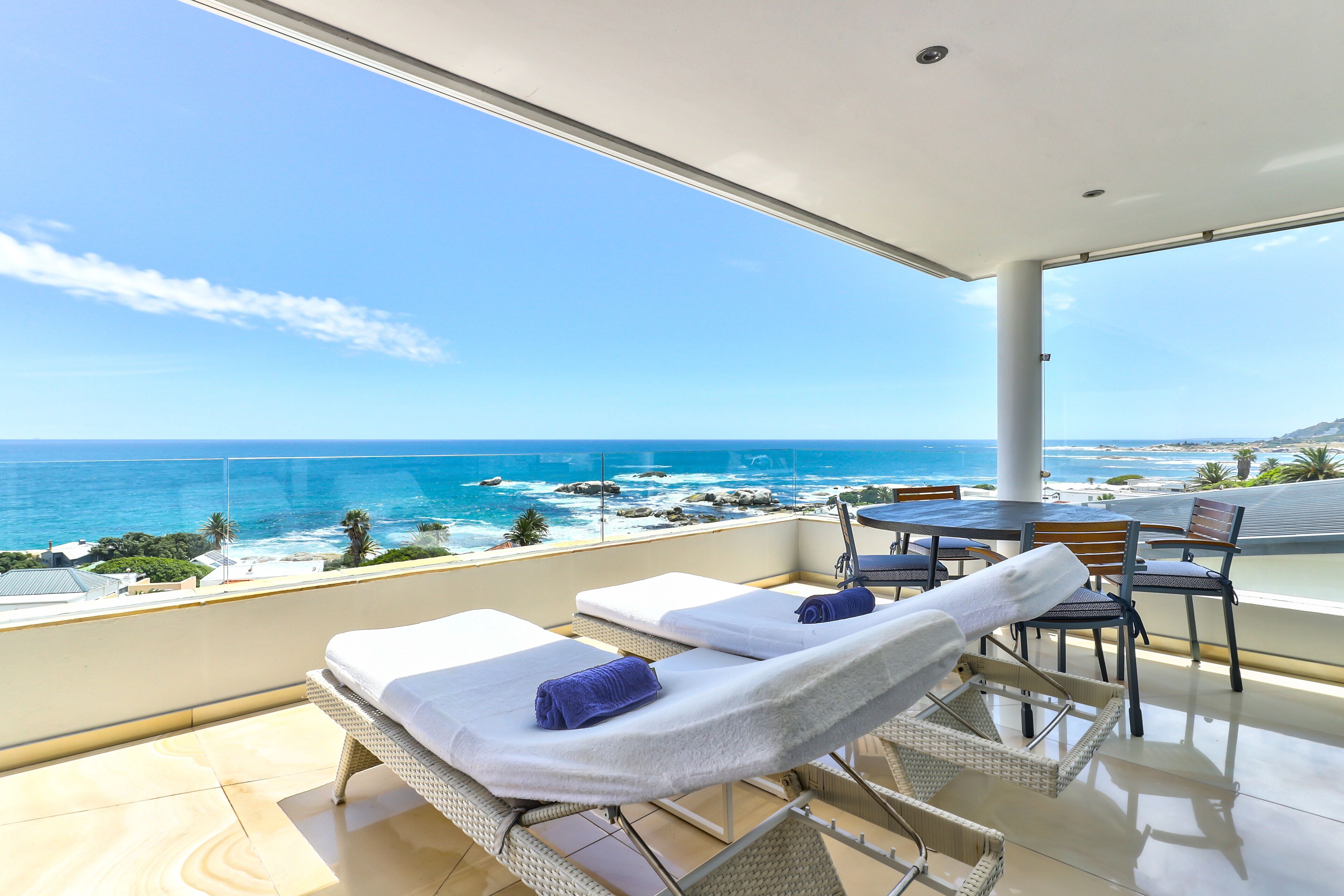 Varanda com duas espreguiçadeiras, uma mesa e cadeiras, com vista para o oceano.