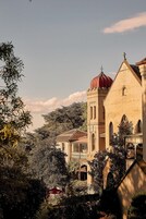 Igreja com uma cúpula vermelha imponente e um campanário, rodeada por vegetação exuberante e outros edifícios.