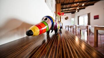 Uma escultura abstrata e colorida sobre uma mesa de madeira, num espaço com teto de madeira e paredes brancas.
