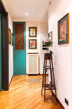 Um corredor com piso de madeira, porta verde-água e quadros nas paredes.