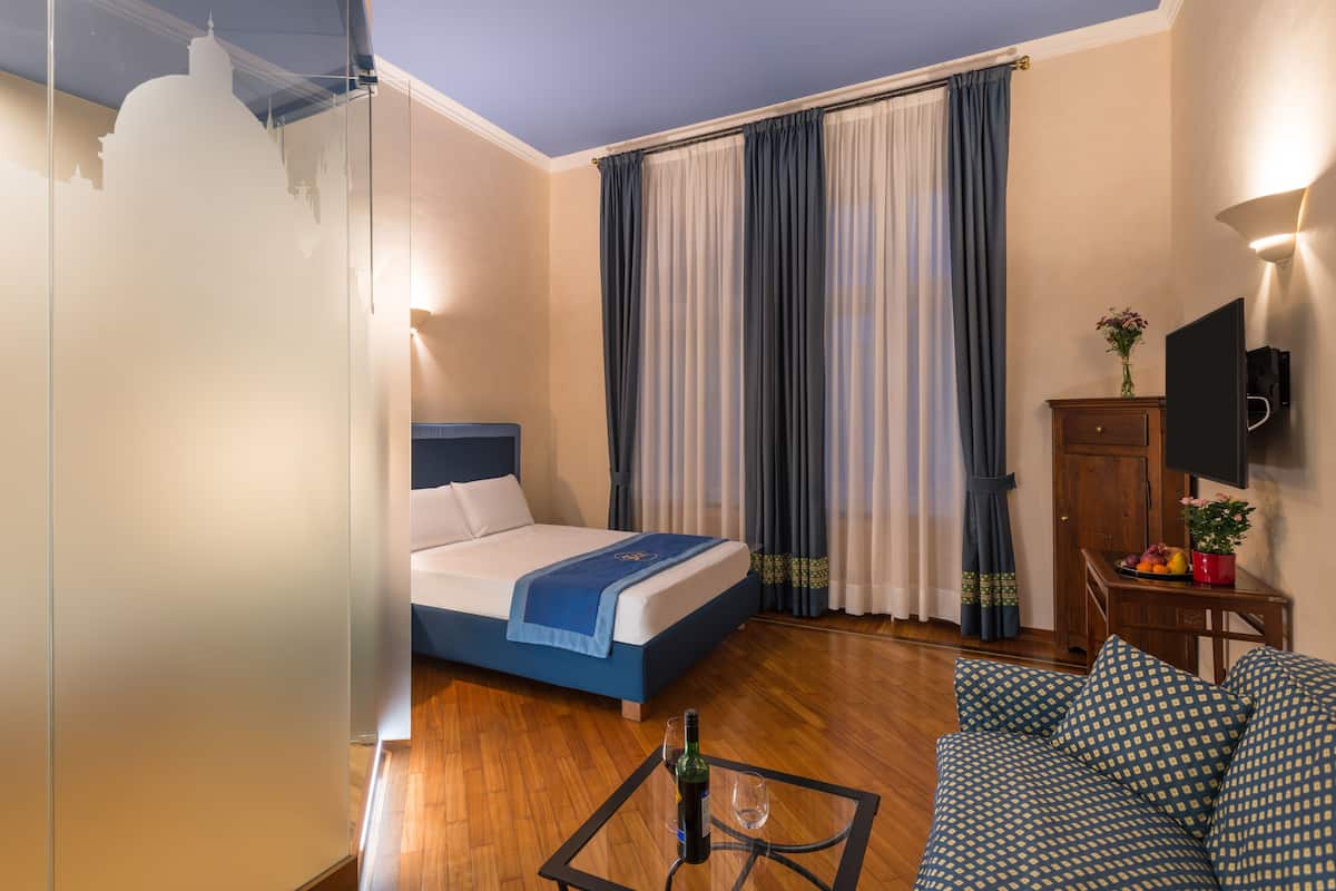 Quarto de hotel com cama, sofá, televisão, armário de madeira e janela com cortinas.