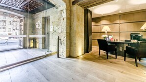 Um saguão com porta de vidro, piso de madeira e um balcão de recepção com duas cadeiras.