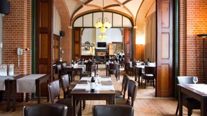 Um restaurante com paredes de tijolo, mesas e cadeiras de madeira. Há uma lareira ao fundo.