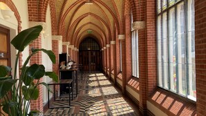 Um longo corredor com tetos em arco e ladrilhos estampados, que leva a uma área central com mesas e cadeiras.