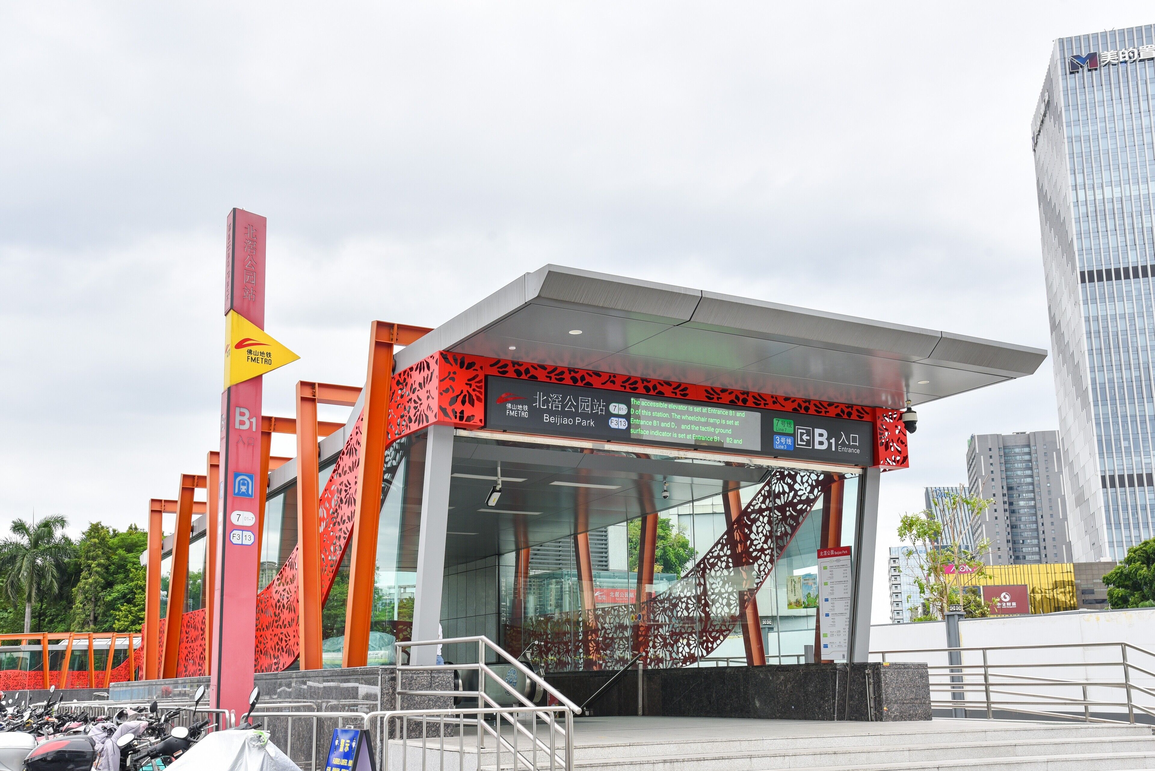 Uma estação de trem moderna com fachada distinta em vermelho e preto, sinalização clara para Beijing Park e vista dos edifícios ao redor.