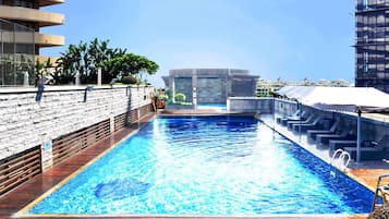 Piscina no terraço com deck de madeira, cercada por edifícios e vegetação.