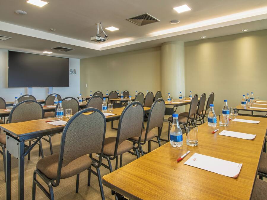 Uma sala de conferências com várias mesas, cadeiras e uma tela grande.