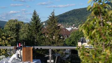 Mesa de jantar com cadeiras e copos de vinho, com vista para uma cidade com casas e uma colina ao fundo.