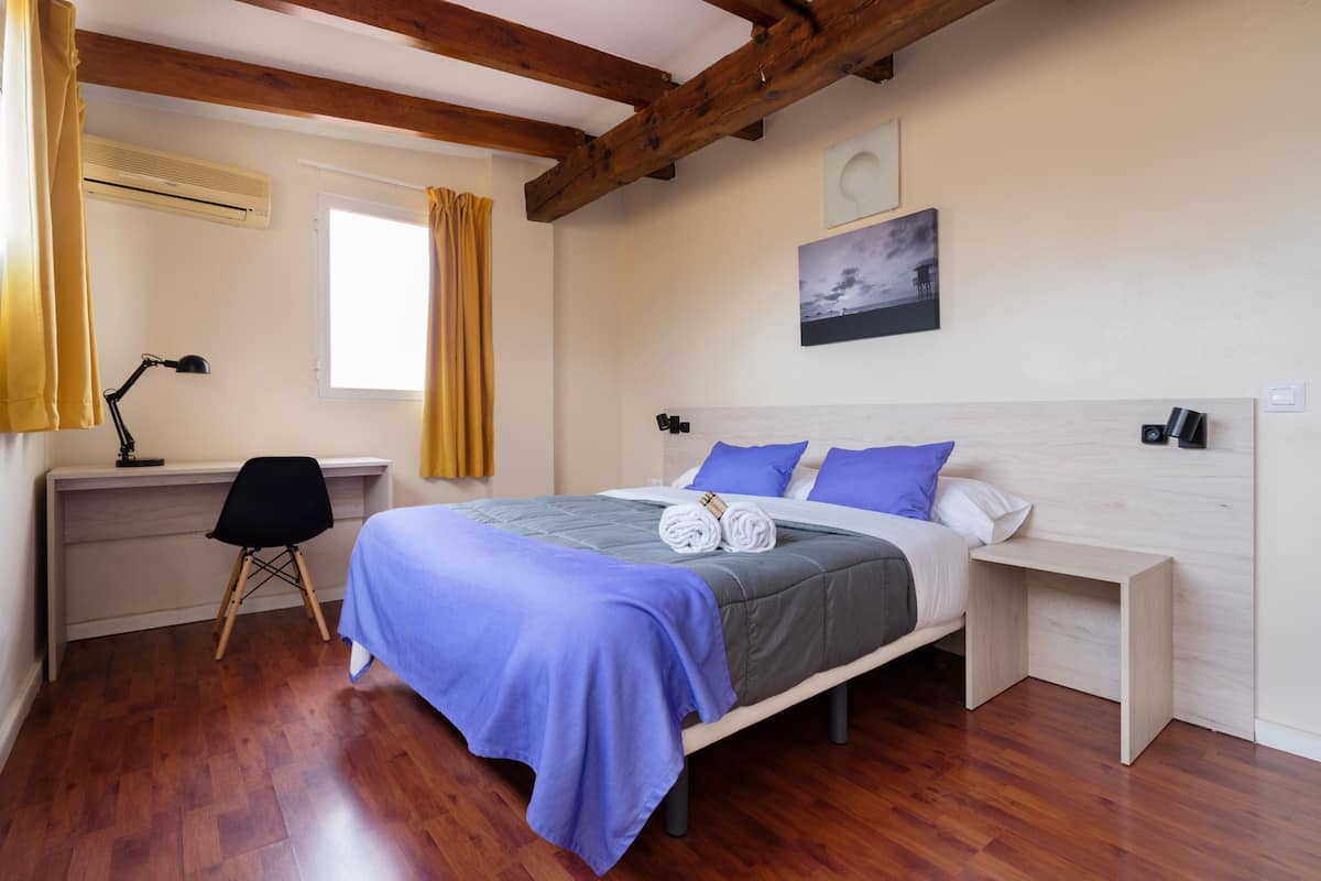 Quarto com uma cama, escrivaninha, cadeira e janela com cortinas.
